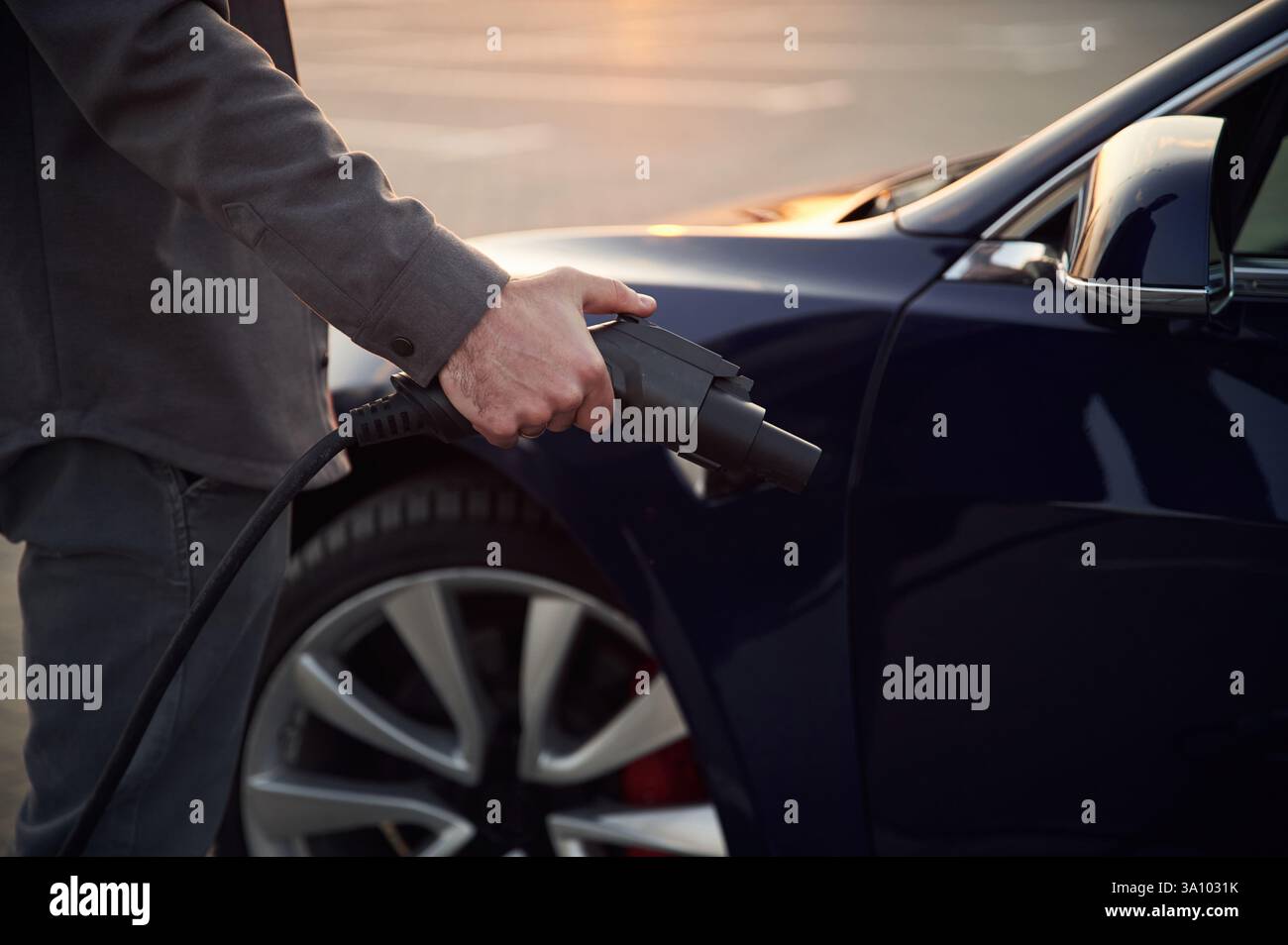 Putting charger into socket. Man is standing near his electric car ...