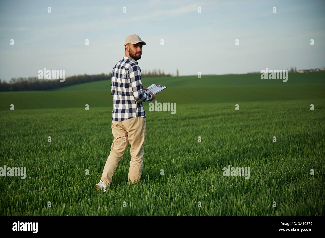 Walking, holding notepad. Handsome young man is on agricultural field ...