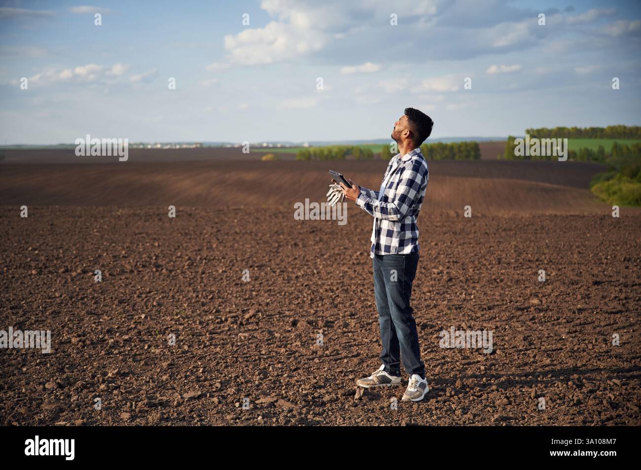Standing on cultivated agricultural field with tablet. Handsome Indian ...