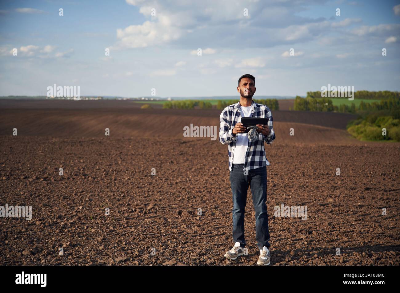 Standing on cultivated agricultural field with tablet. Handsome Indian ...