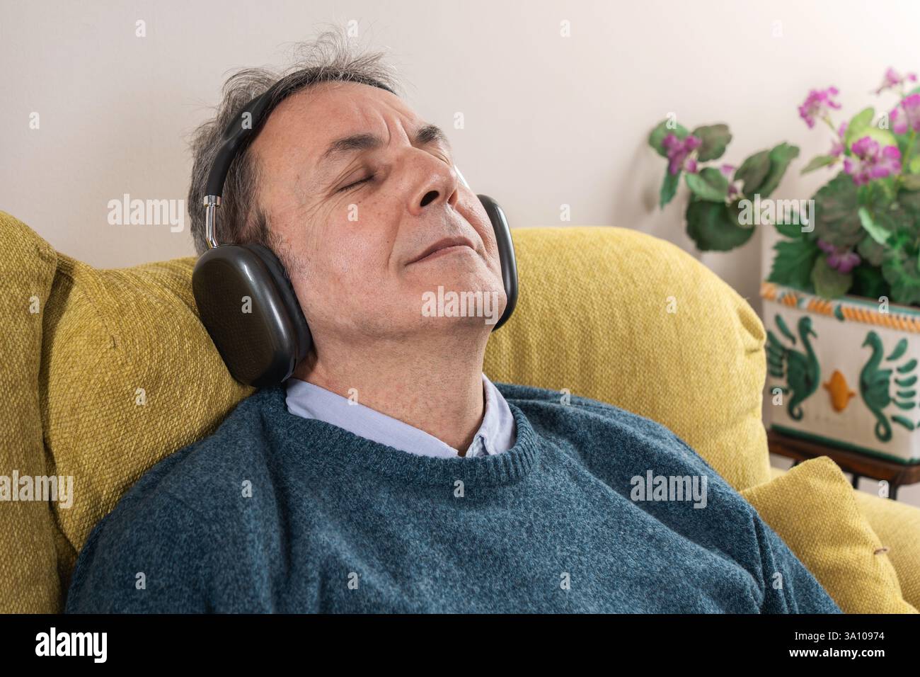 Senior man wearing wireless headphones, sitting on a couch with eyes ...