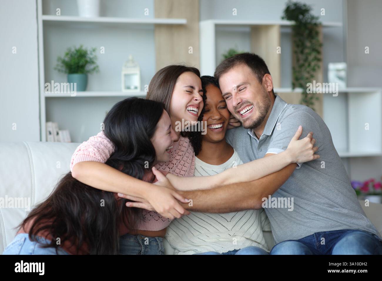 Four happy friends or roommates hugging sitting on a couch at home ...