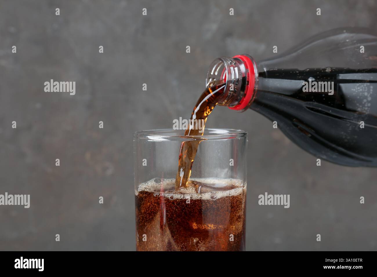 Pouring refreshing cola from bottle into glass on blurred grey ...