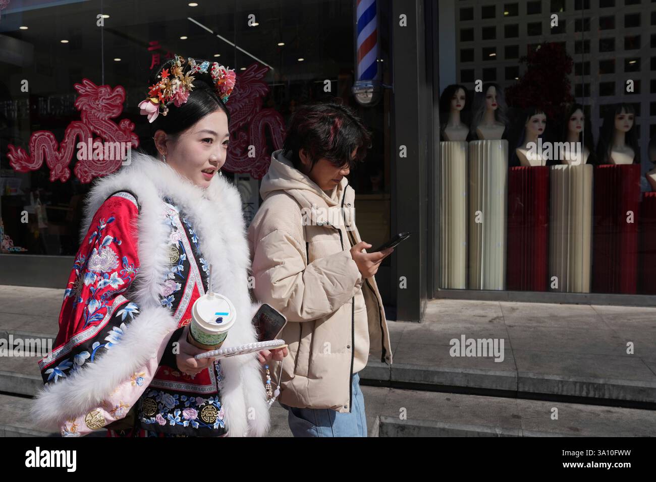 A woman wearing traditional costume passes by stores along the popular ...