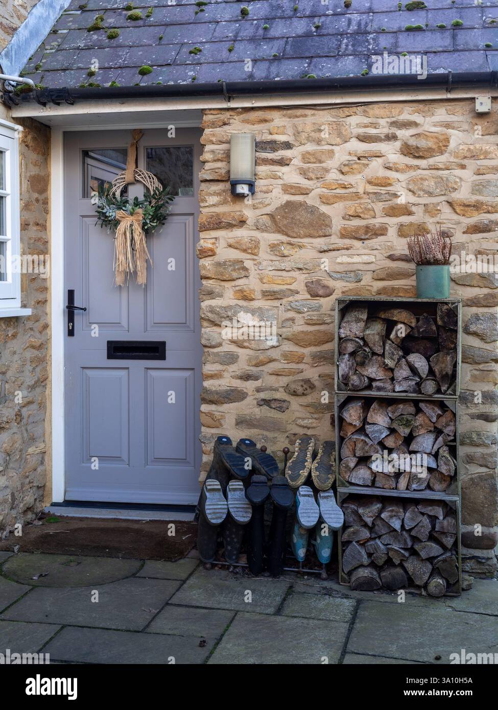 Back door to an old stone built cottage with log store and boot rack in ...