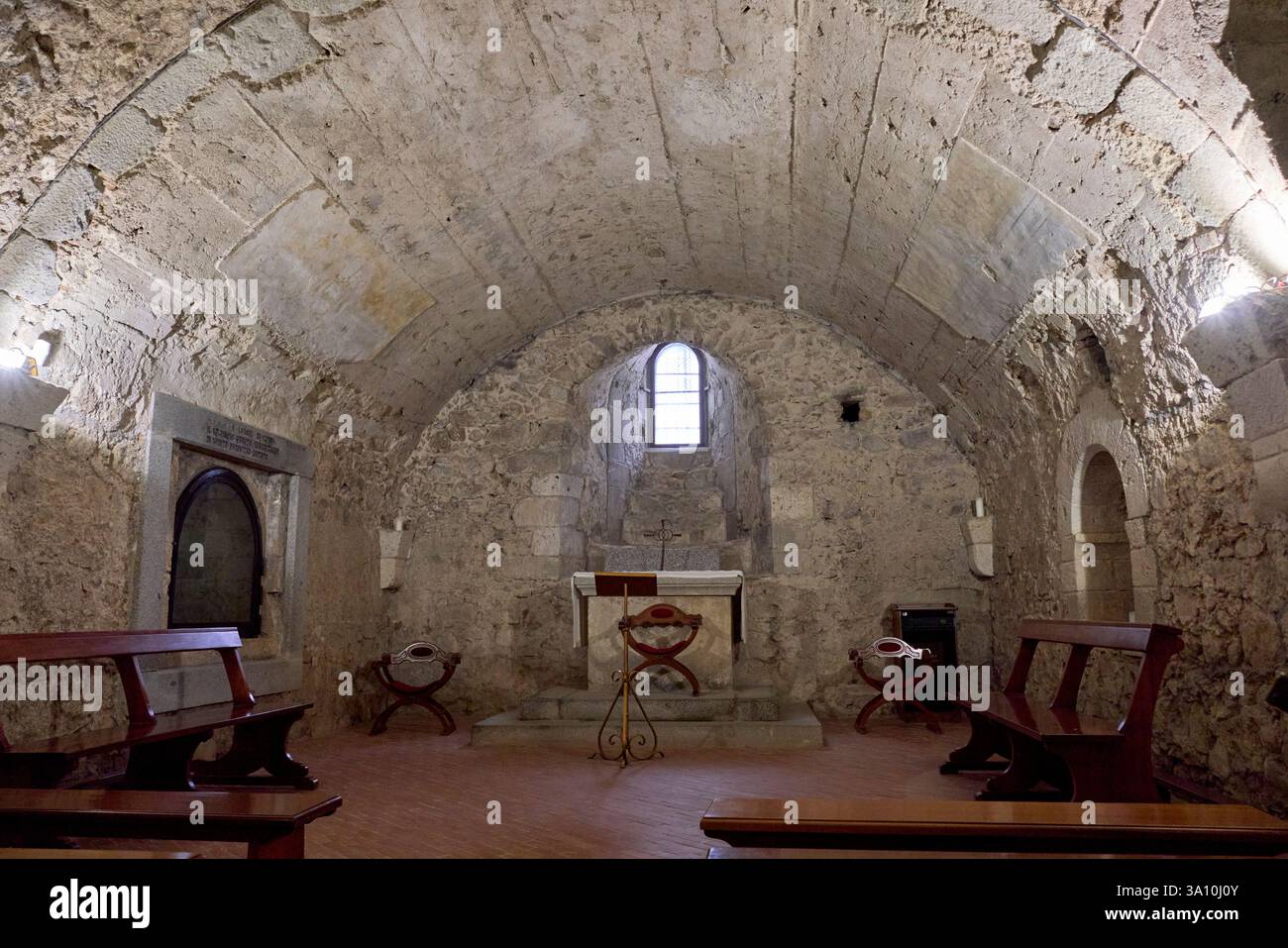 Ancient stone chapel interior with arched ceiling and wooden pews ...