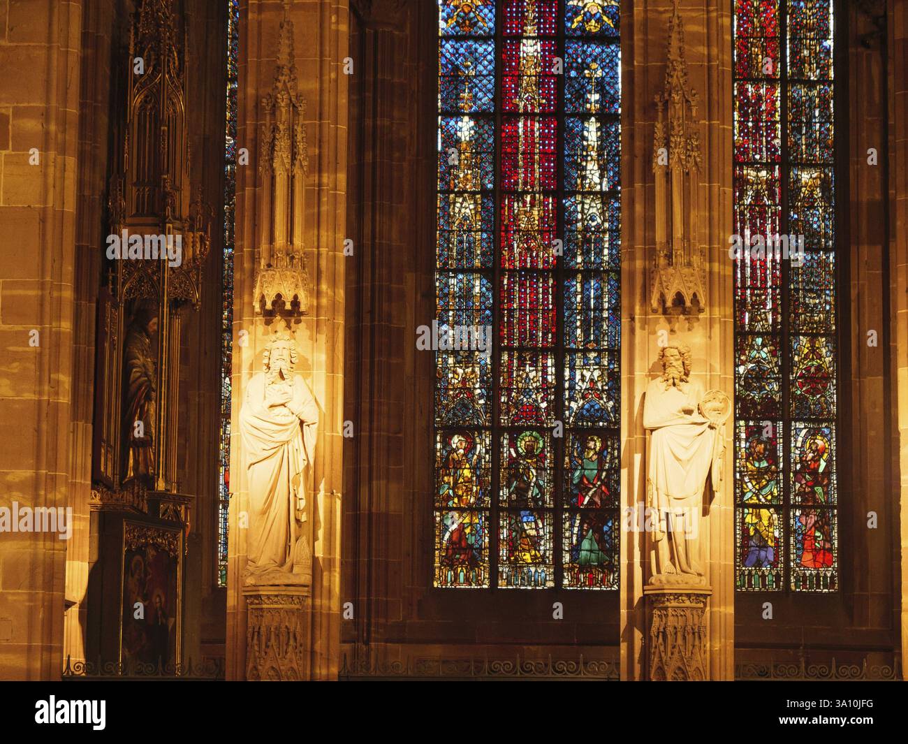 Statues in a cathedral, flanked by colourful stained glass windows ...