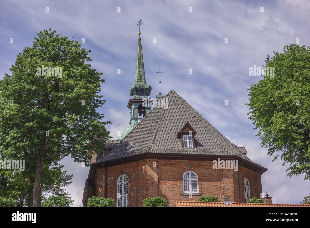 An old brick church tower with a copper spire, surrounded by green ...
