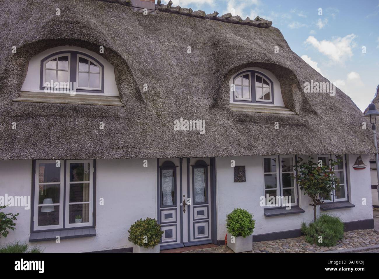 Cosy house with thatched roof and ornate windows under a blue sky ...