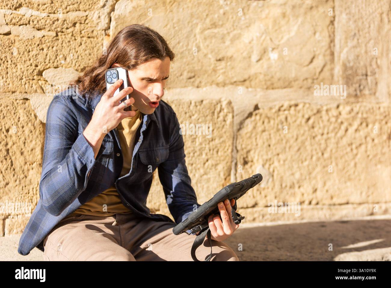 Frustrated man talking on smartphone while using a rugged tablet ...