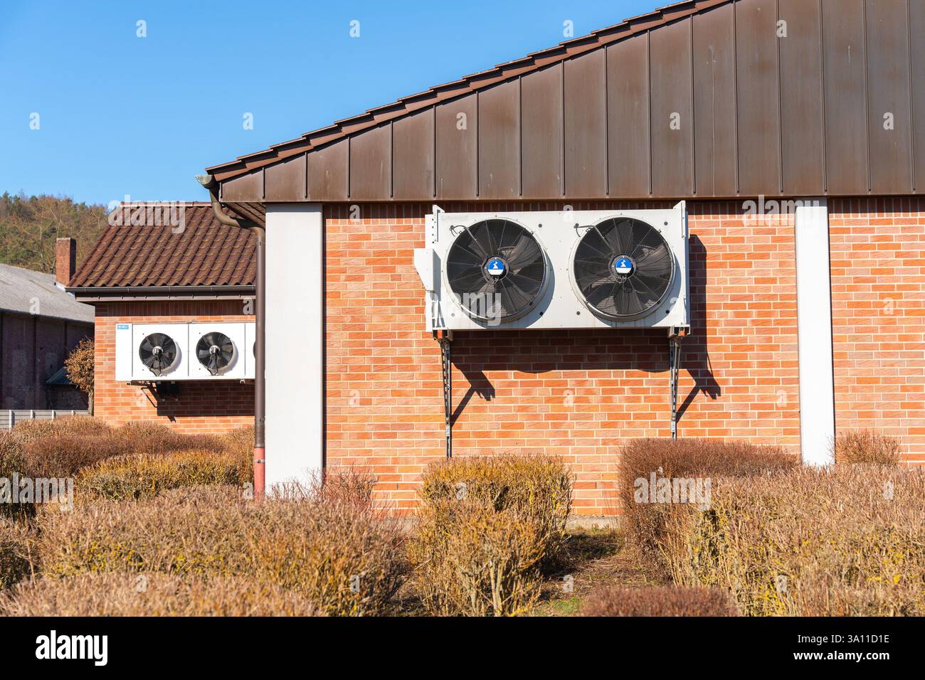 Two large electric fans are fixed on a red brick wall, supported by ...