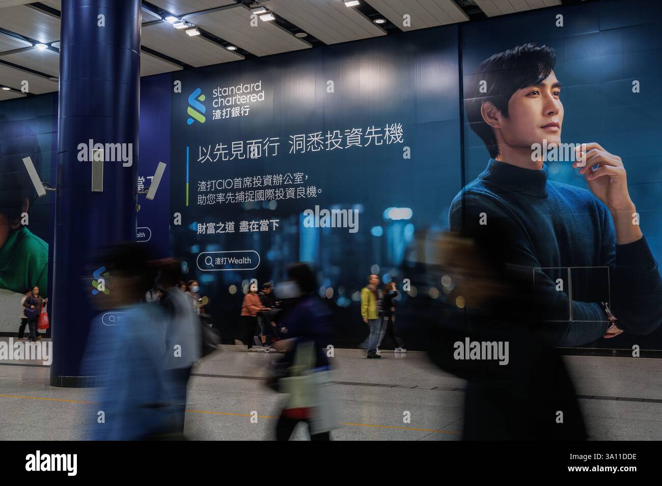 People walk past a large advertisement for Standard Chartered Bank in ...