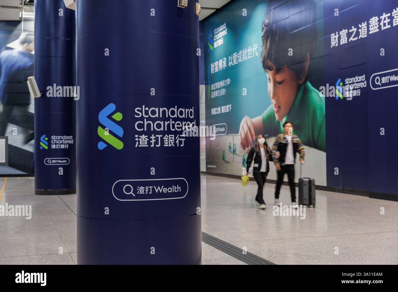 People walk past a large advertisement for Standard Chartered Bank in ...