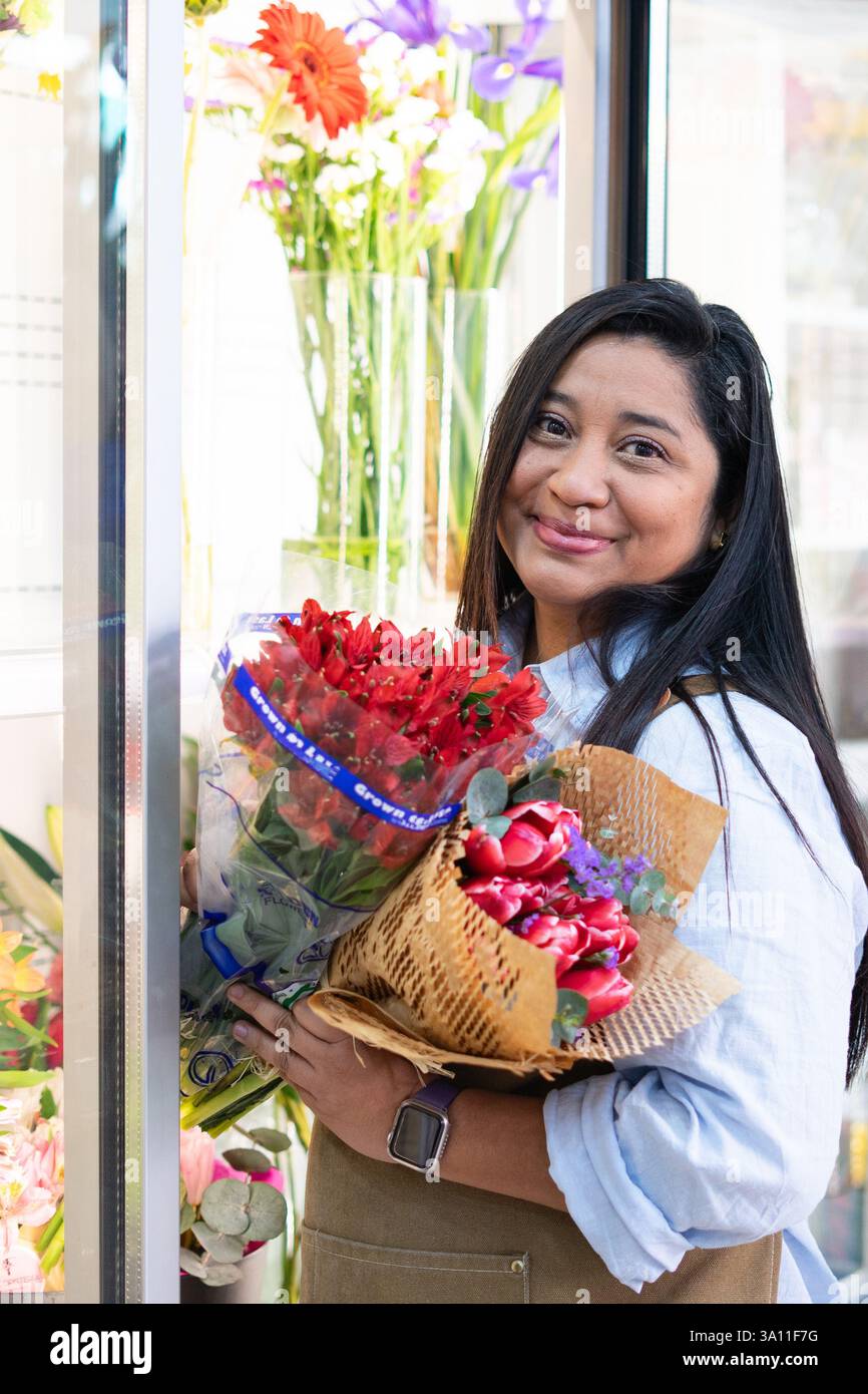 Latin florist holding bouquets of fresh red and pink flowers, smiling ...