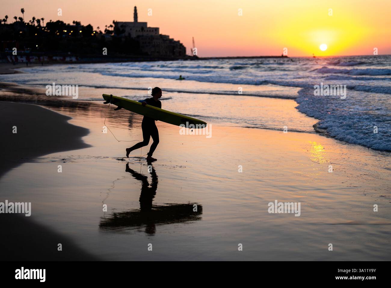FILE - A surfer goes into the Mediterranean sea as the sun sets behind ...