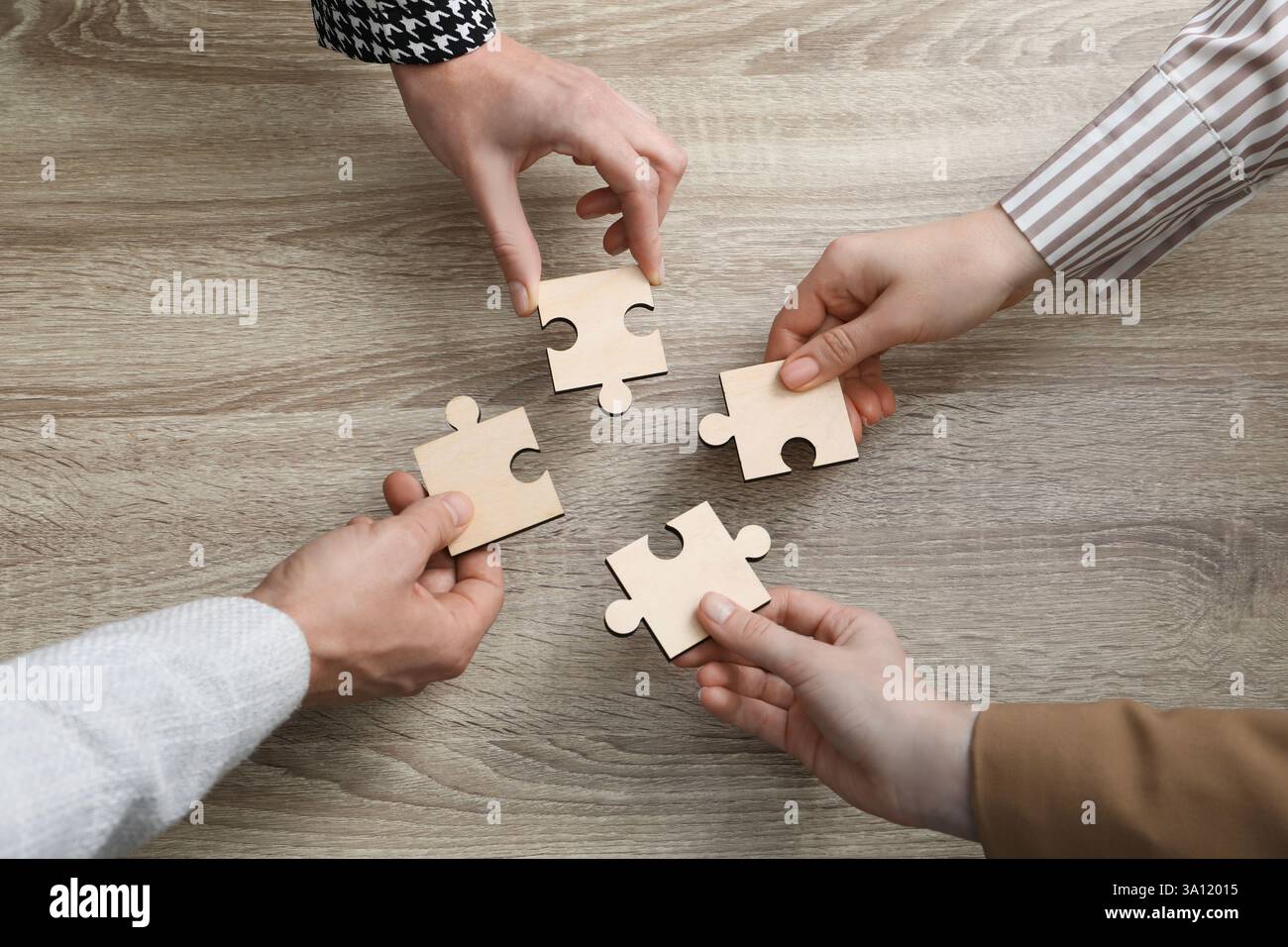 Teamwork. Group of people putting puzzle pieces together at wooden table, top view Stock Photo ...