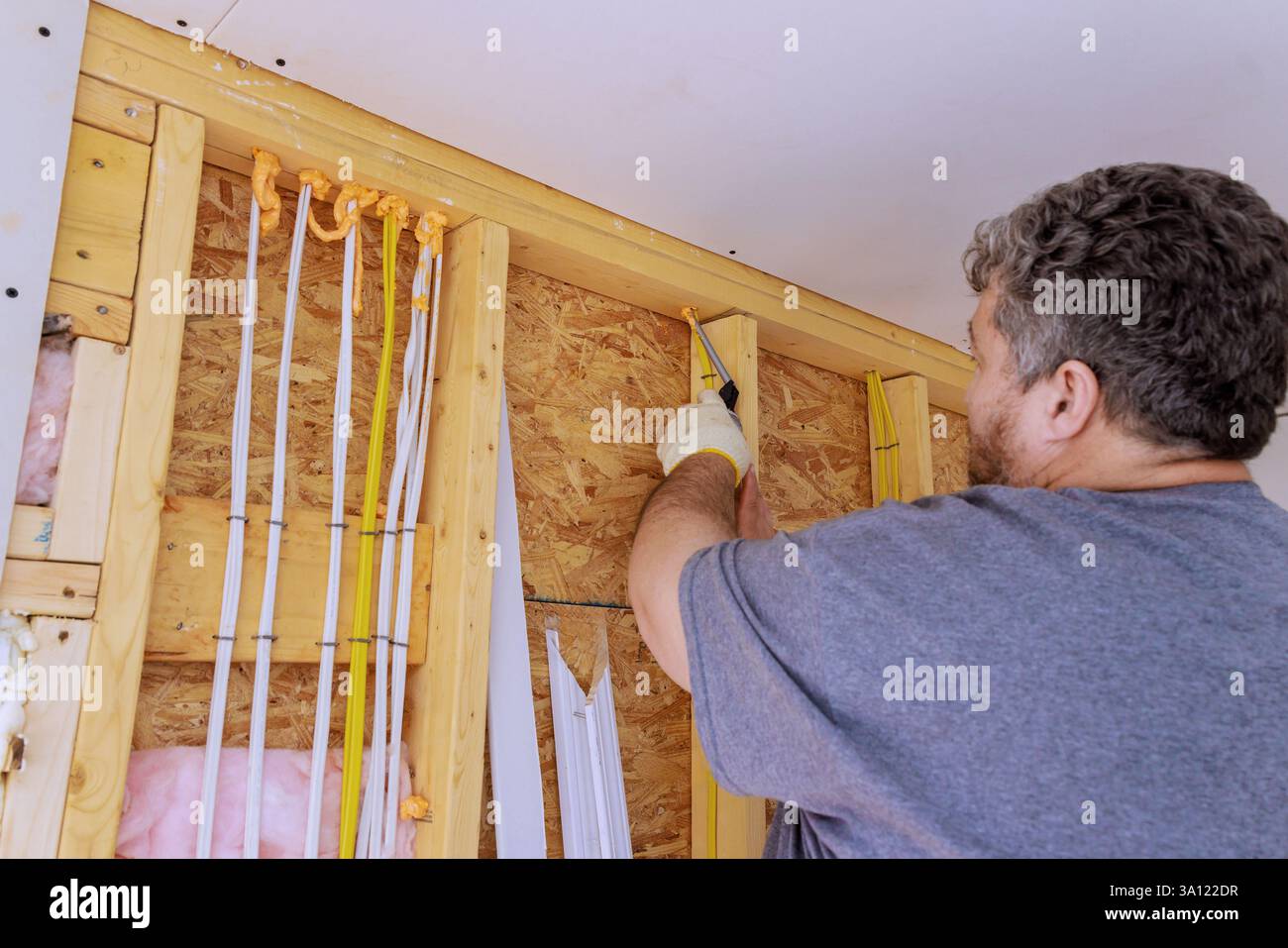 Worker applies foam insulation prepares electrical wiring in home renovation on improving energy ...