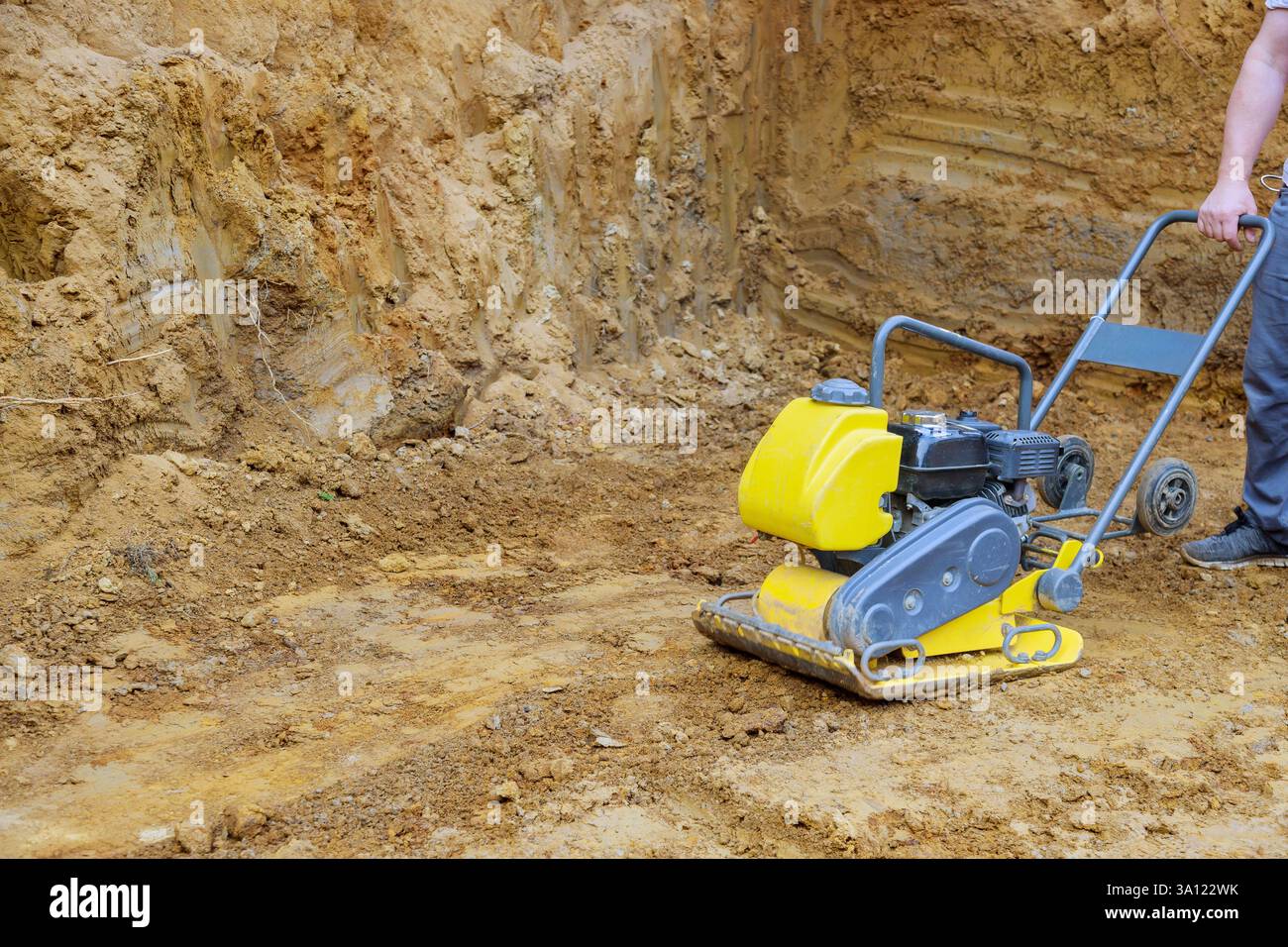 Worker operates yellow compactor to flatten soil in construction area ...