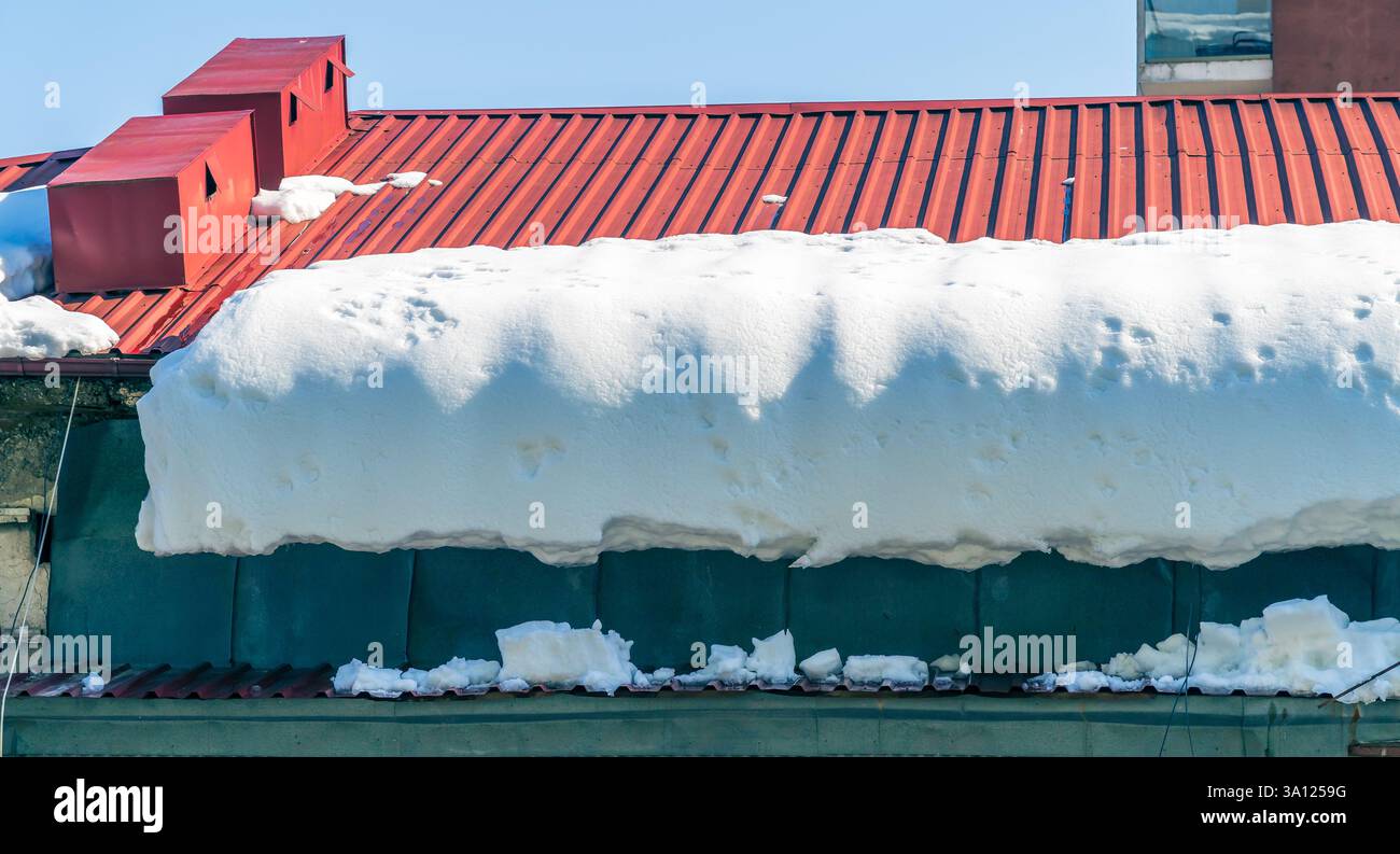 Large snowdrift melting on red metal roof creating risk of collapse and ...