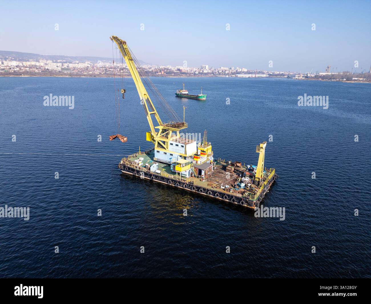 A floating crane barge with a large yellow crane operates on calm ...