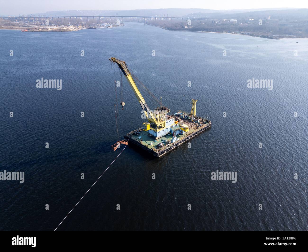 A floating crane barge with a large yellow crane operates on calm ...