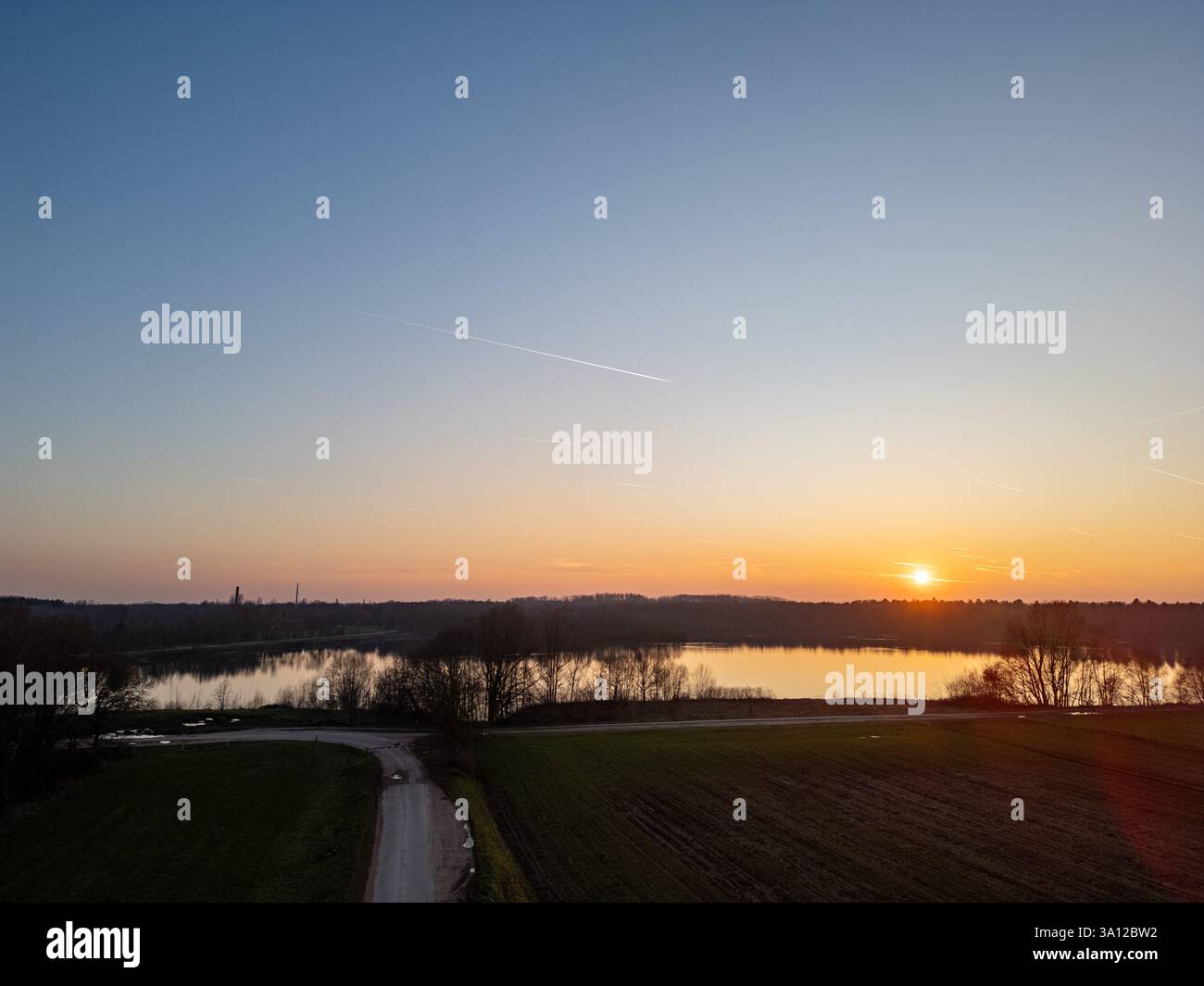 A stunning sunset reflects on a calm lake, surrounded by lush greenery ...