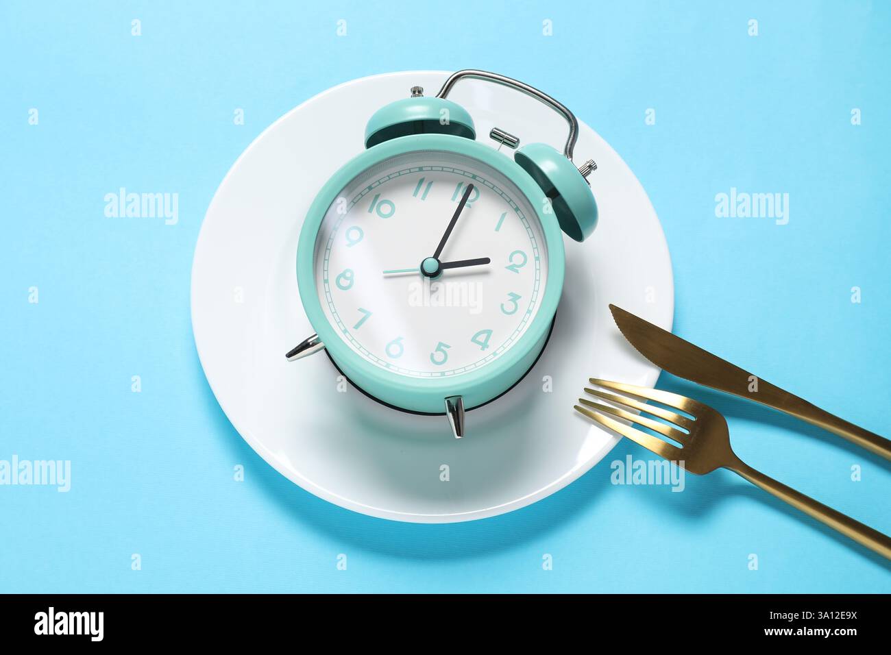 Time for meal. Alarm clock, plate and cutlery on light blue background ...