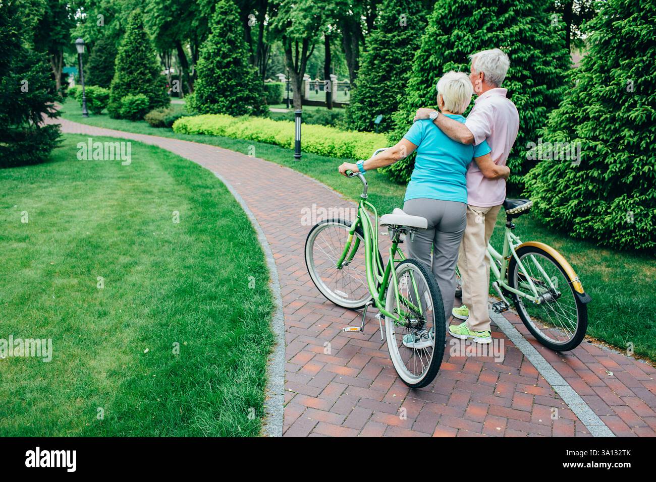 A senior couple takes a break on their bicycles, embracing in a peaceful park surrounded by ...