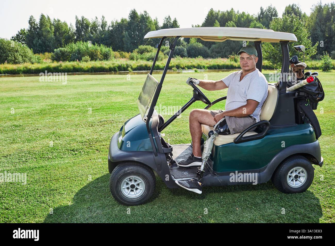 A man with a prosthetic leg drives a golf cart across the lush green ...