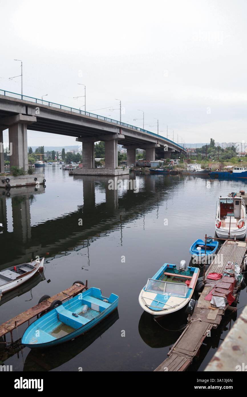 Quiet riverside with small boats below an elevated bridge. A serene ...