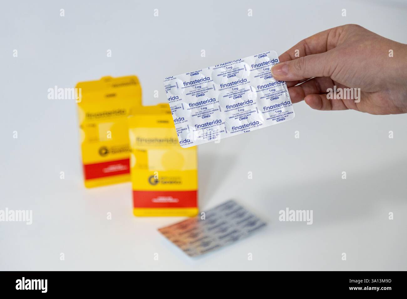 Hand holding a blister pack of Finasteride 1mg with medication boxes in ...