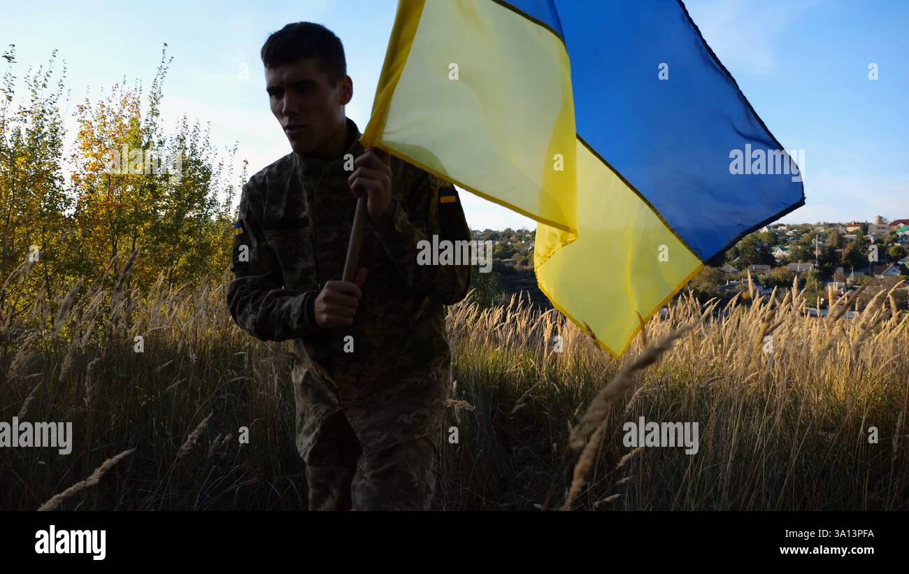 Young male military in uniform walks with waving flag of Ukraine at ...