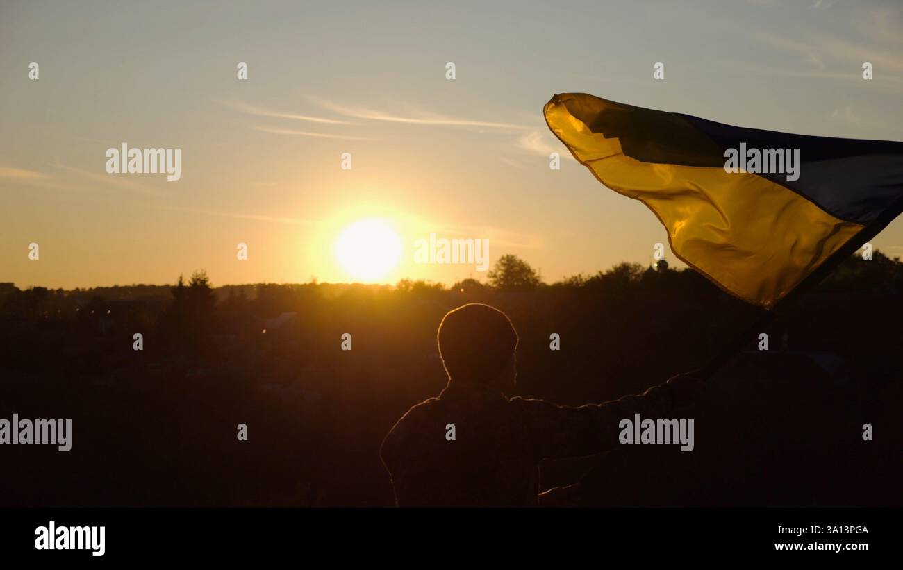 Young man in military uniform waving flag of Ukraine against beautiful ...