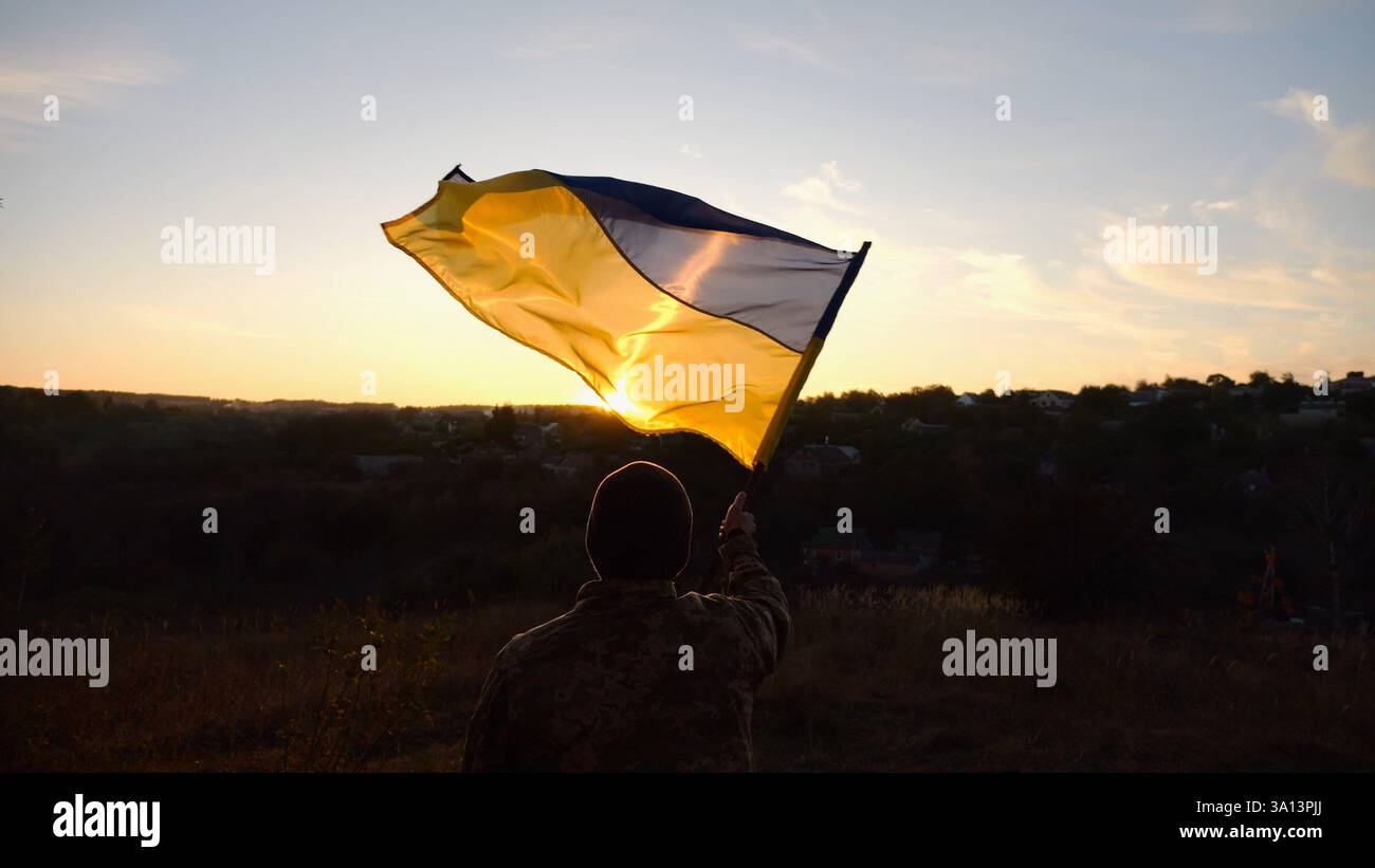 Young man in military uniform waving flag of Ukraine against beautiful ...