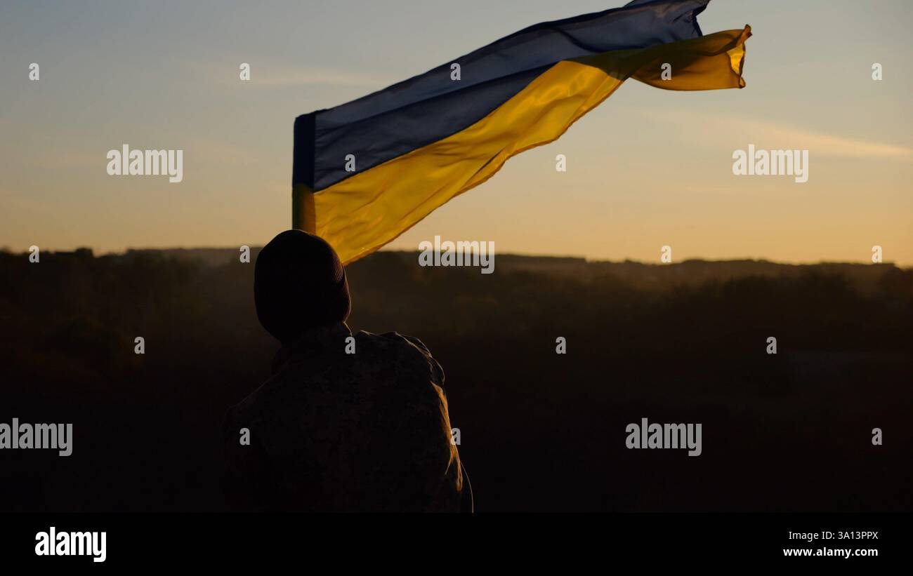 Young man in military uniform waving flag of Ukraine against beautiful ...