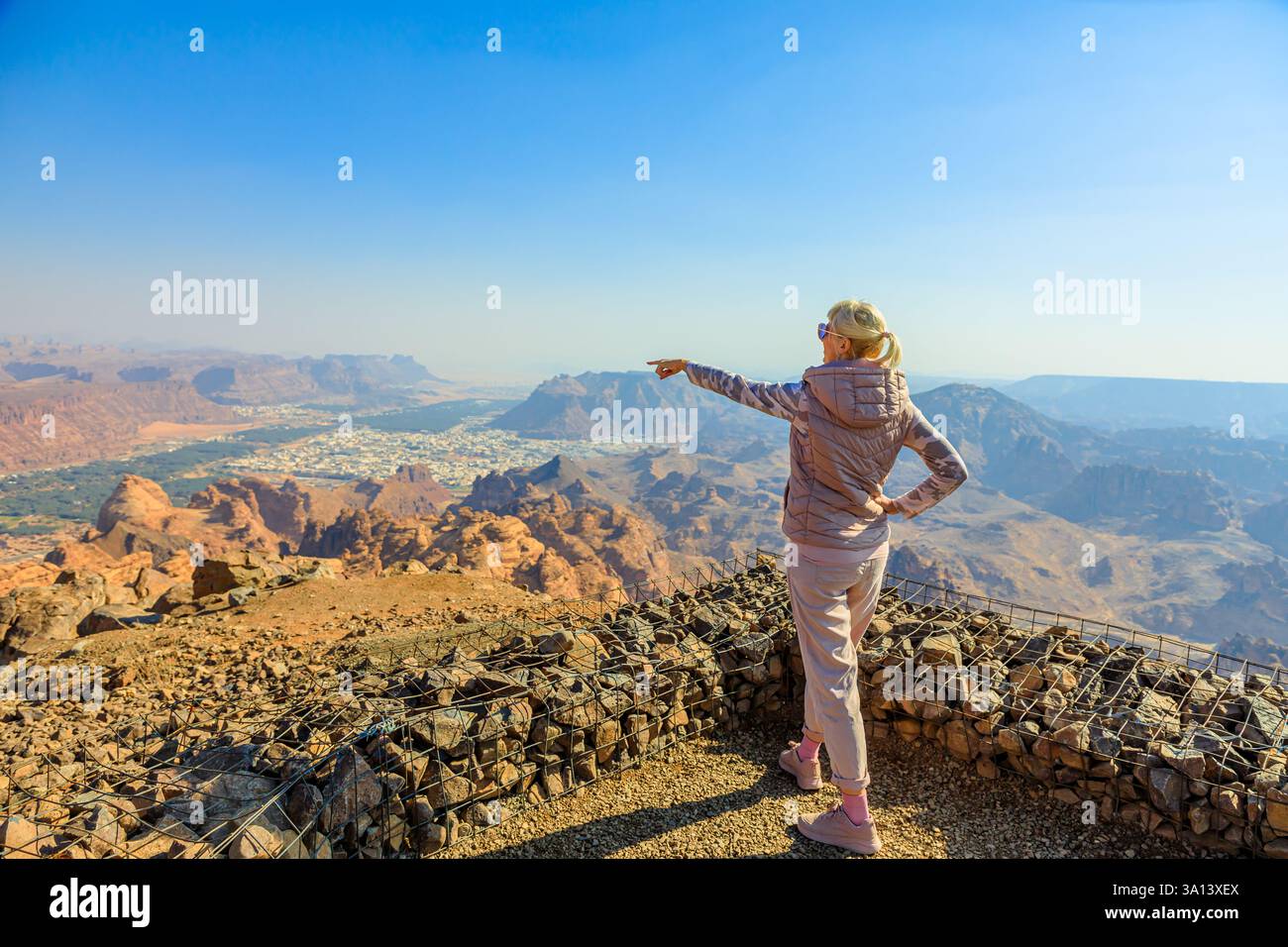 Blonde tourist pointing at AlUla Old Town from the Harrat Viewpoint ...