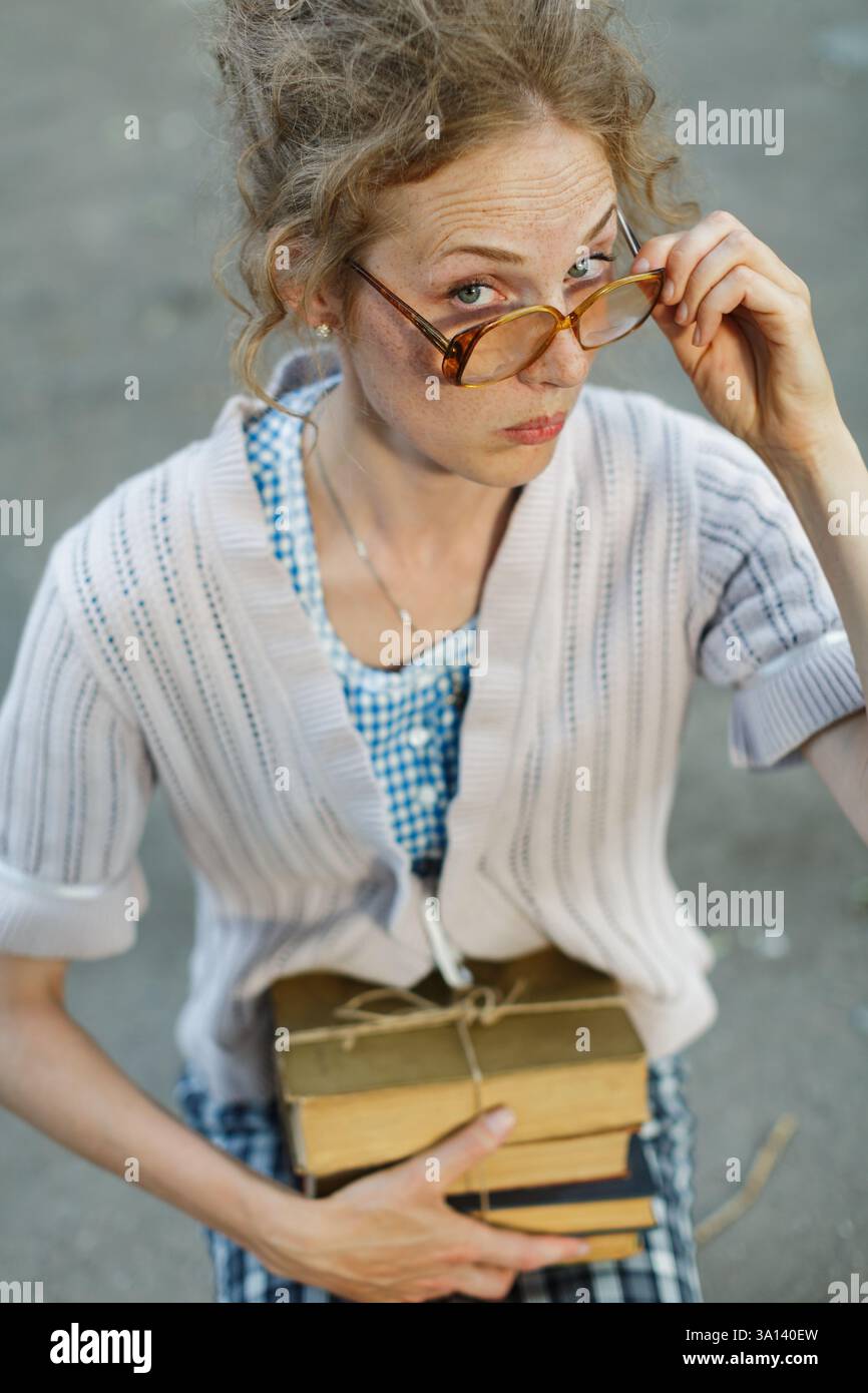 Nerdy young woman in oversized glasses struggles to carry heavy books ...