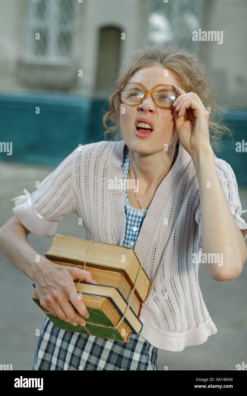 Nerdy young woman in oversized glasses struggles to carry heavy books ...