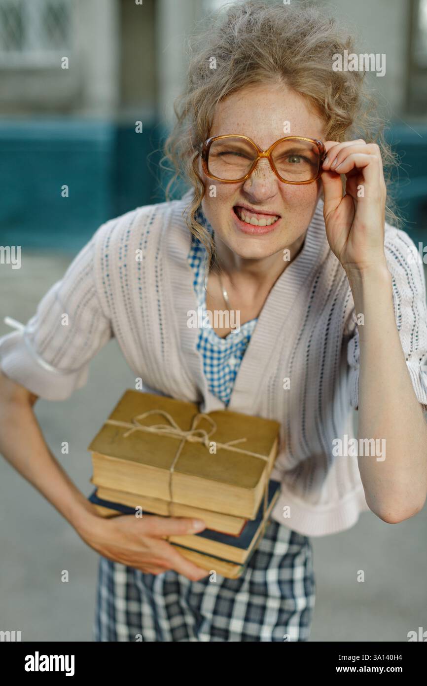 Nerdy young woman in oversized glasses struggles to carry heavy books ...