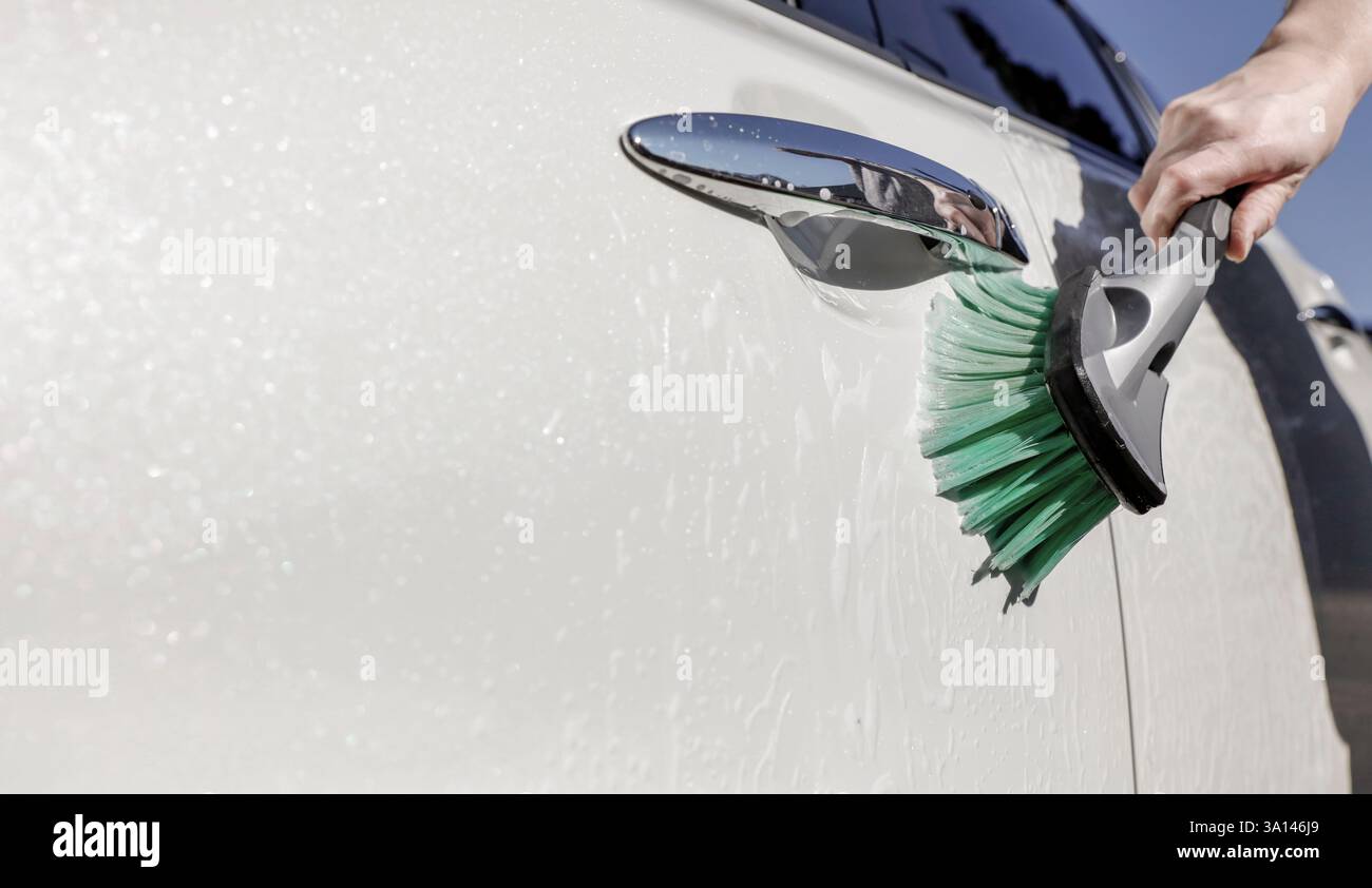 A hand washing the side of a white car using a brush and soapy water ...
