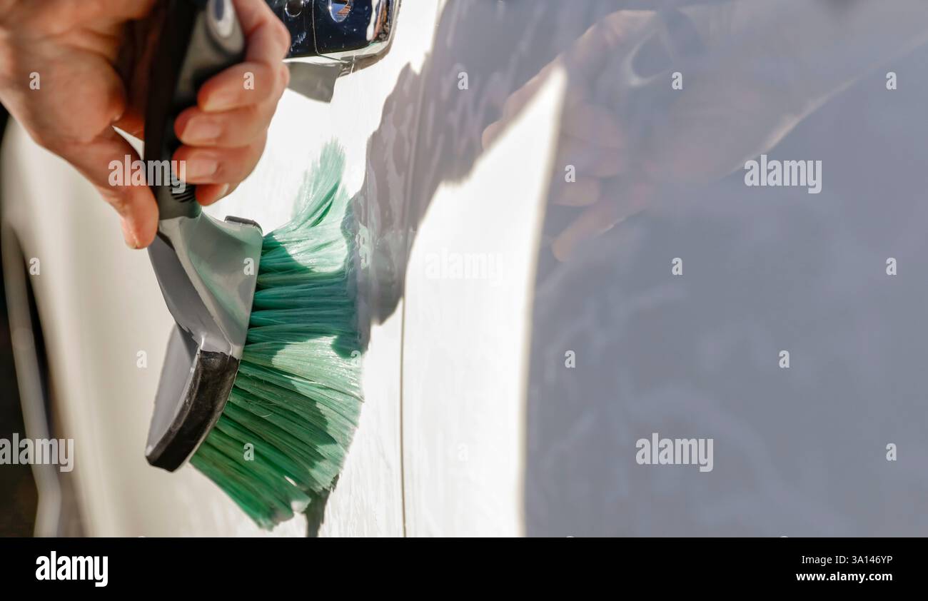 A hand washing the side of a white car using a brush and soapy water ...