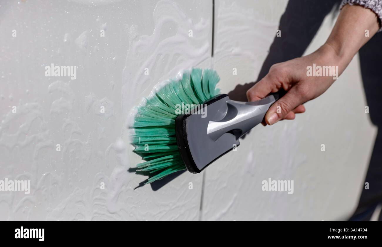 A hand washing the side of a white car using a brush and soapy water ...