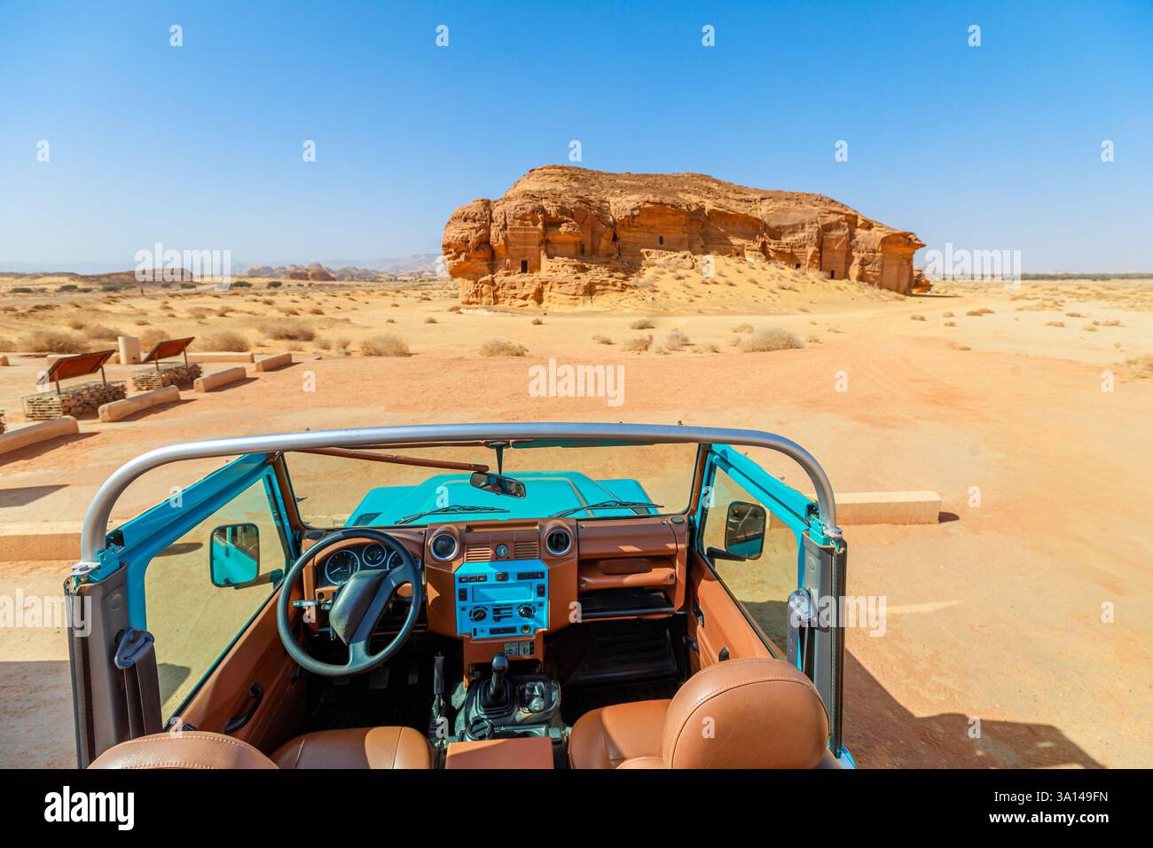 Turquoise SUV beside ancient rock-cut tombs Jabal Al-Ahmar at the Hegra ...