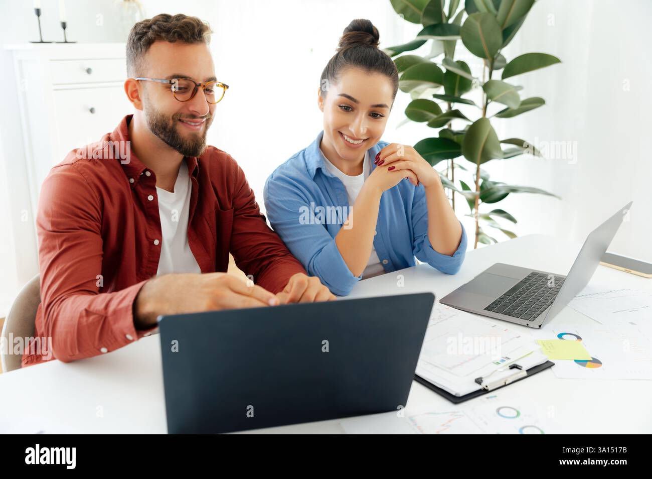 Working process of two successful colleagues working together in an office, sitting at a desk ...