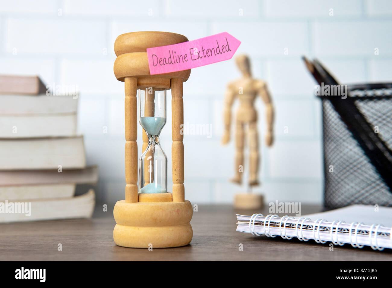 A wooden hourglass and sticky note with the text "Deadline Extended ...