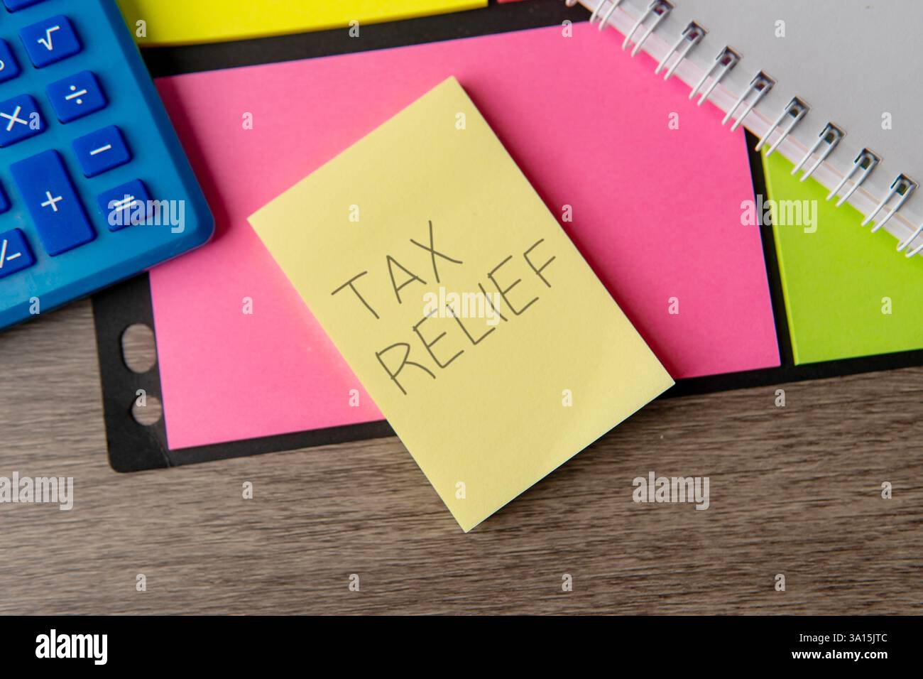 A yellow sticky note with the words "TAX RELIEF" alongside a blue calculator. Financial concept ...