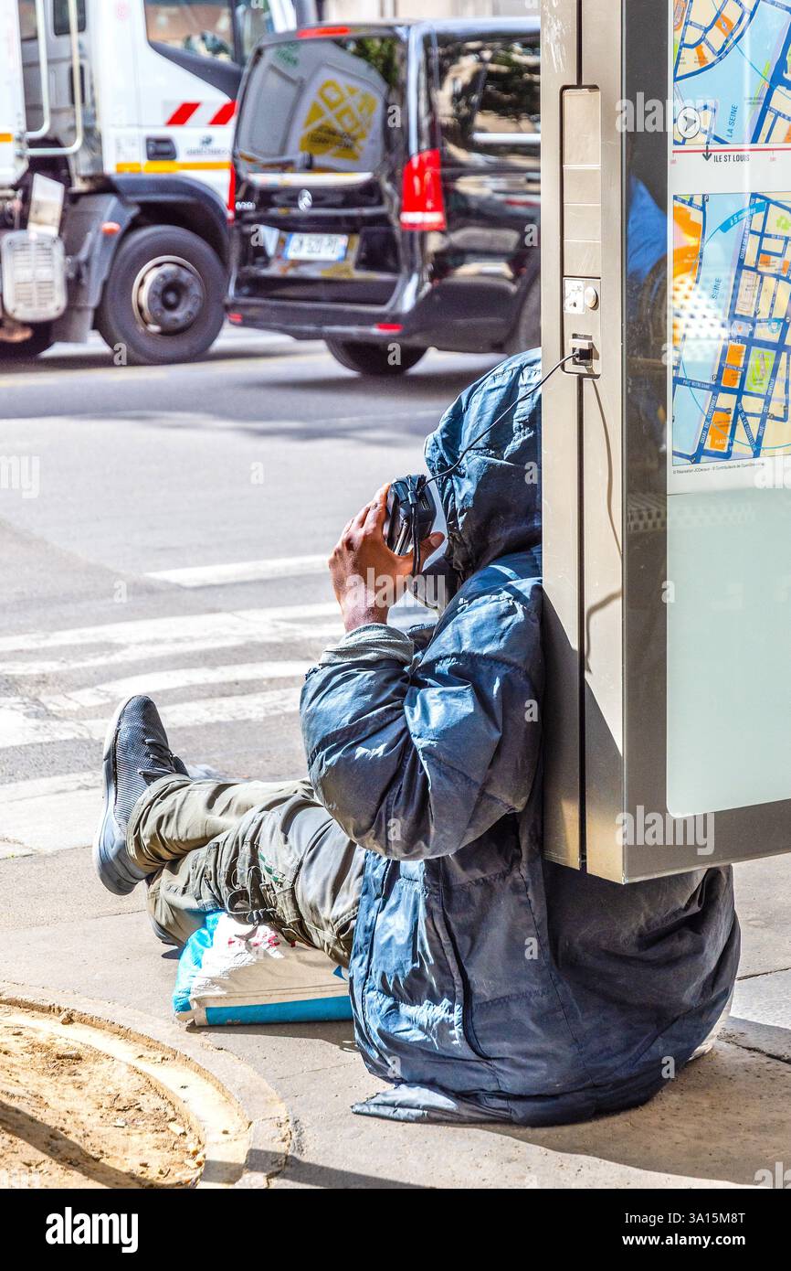 Homeless man sat on pavement charging mobile phone from bus-stop ...