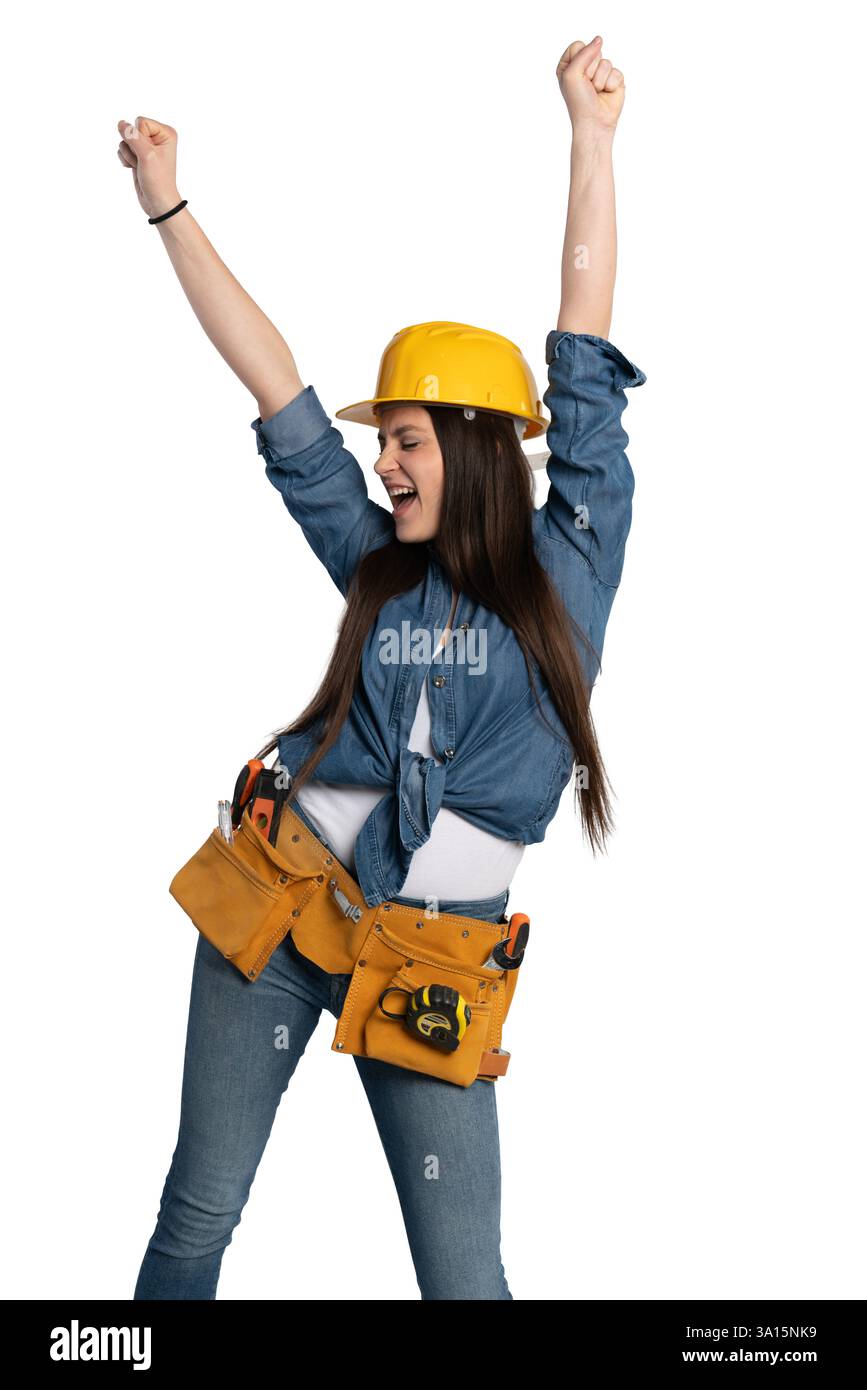 Young female construction worker wearing a yellow hard hat and tool belt, raising her arms in ...