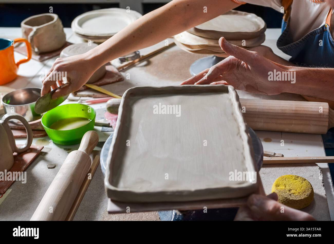 Two potters working together, shaping a clay tray in their pottery ...