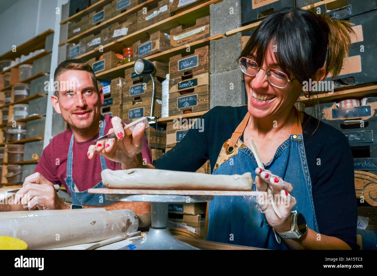 Two craftspeople smiling and shaping clay in their pottery workshop ...
